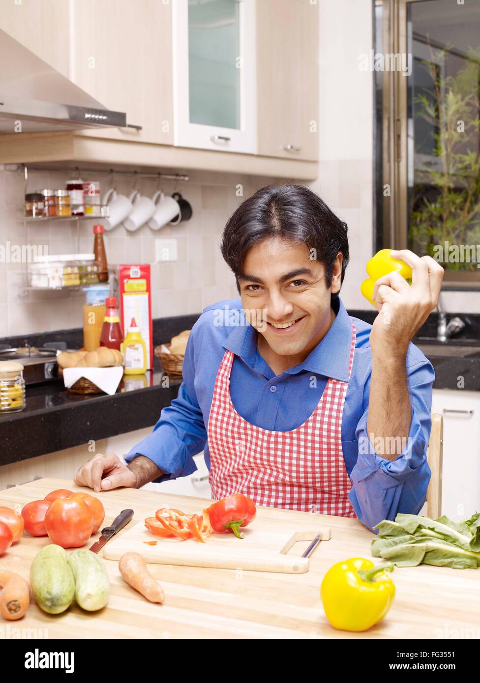 Young man holding capsicum in hand sitting in kitchen MR#702V Stock ...