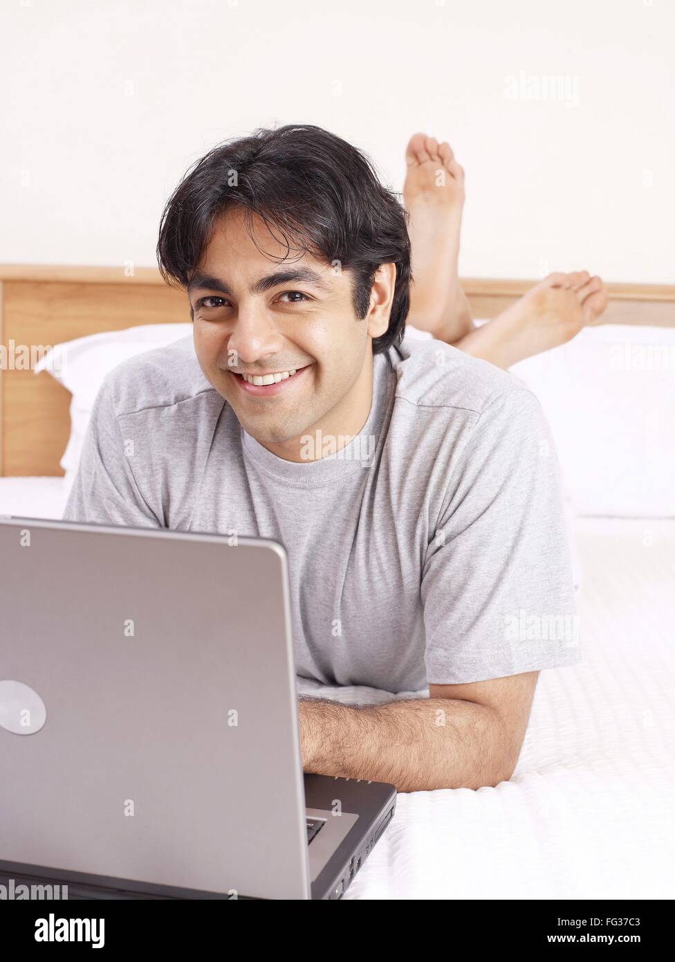 Young man with laptop laying on bed MR#702V Stock Photo - Alamy
