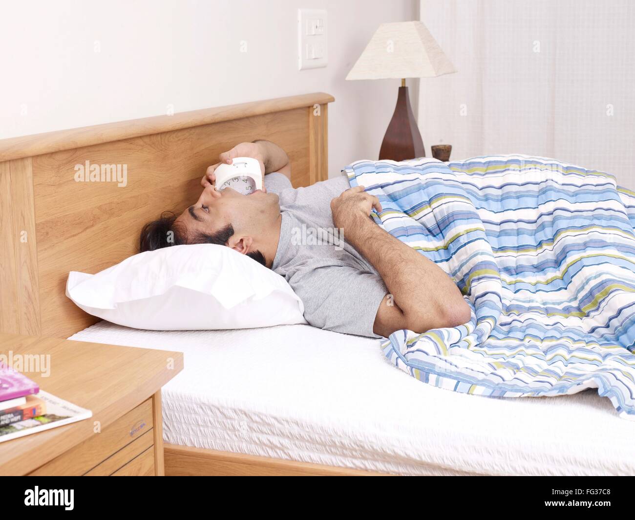 Young man holding alarm clock laying on bed MR#702V Stock Photo - Alamy