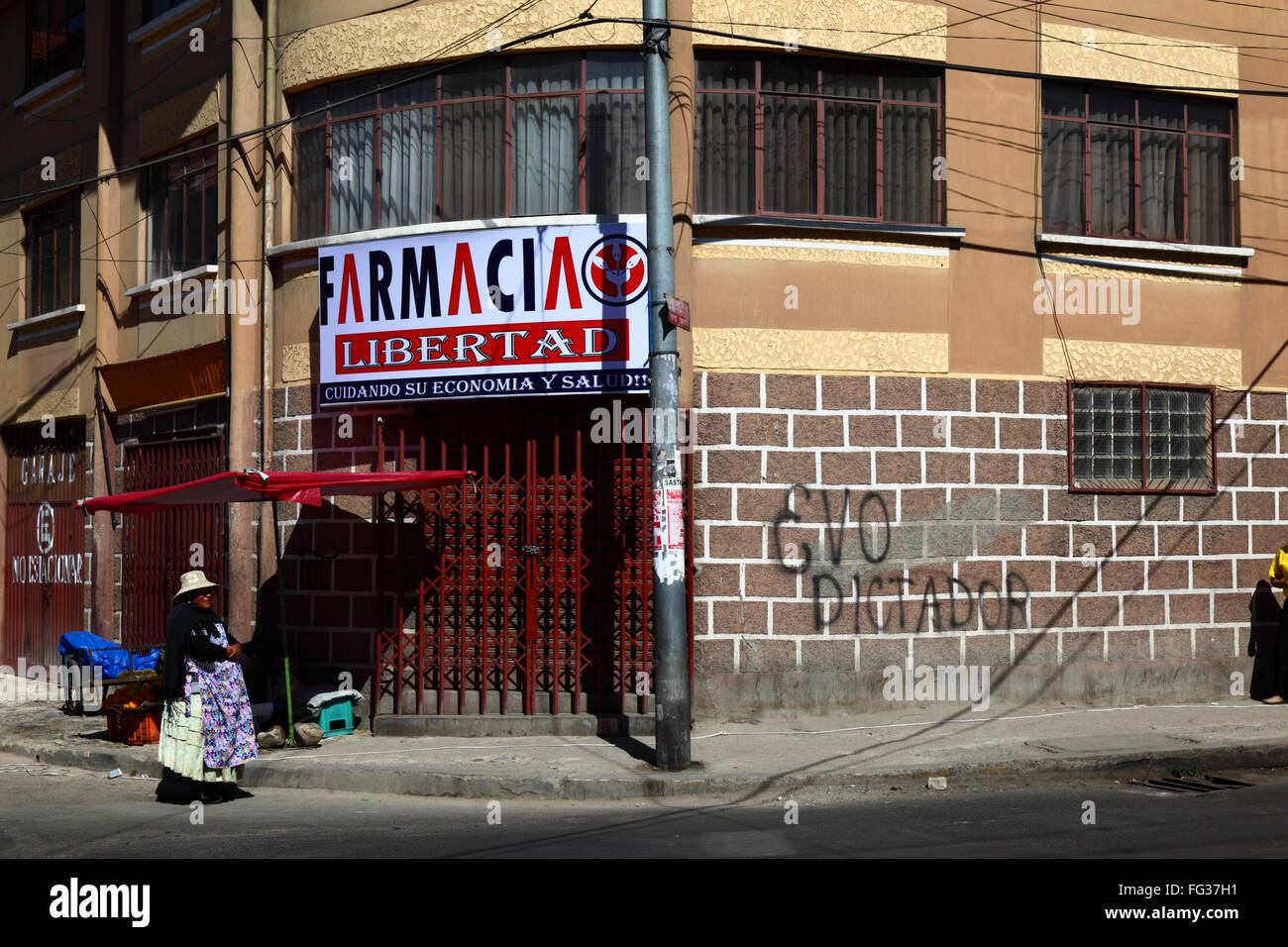 Aymara woman walking past Evo Dictator / Evo Dictator graffiti on wall ...