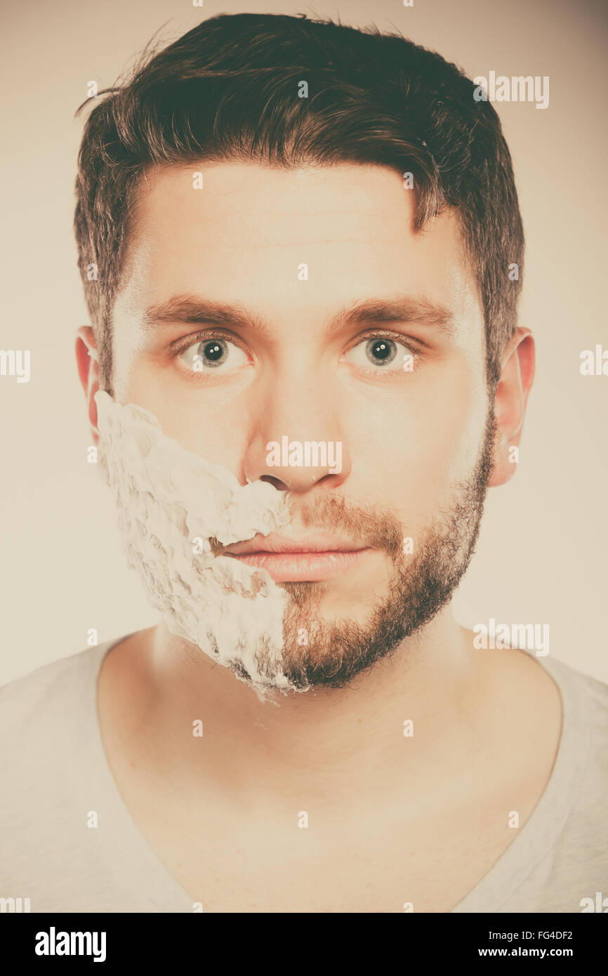 Young man with shaving cream foam on half of face beard. Handsome guy preparing to shave. Skin ...