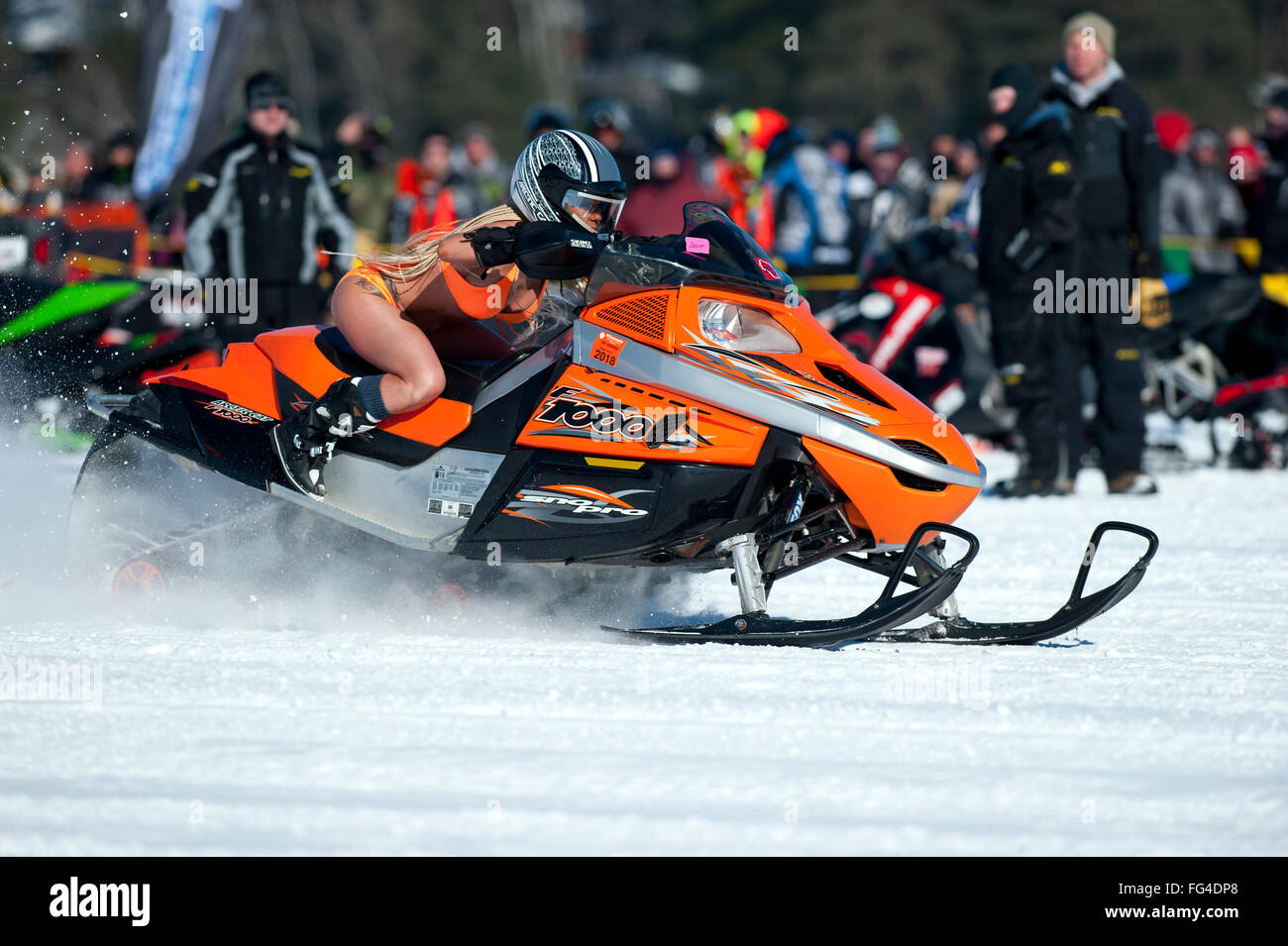 A young woman in a bikini drivers her snowmobile down a ice covered ...