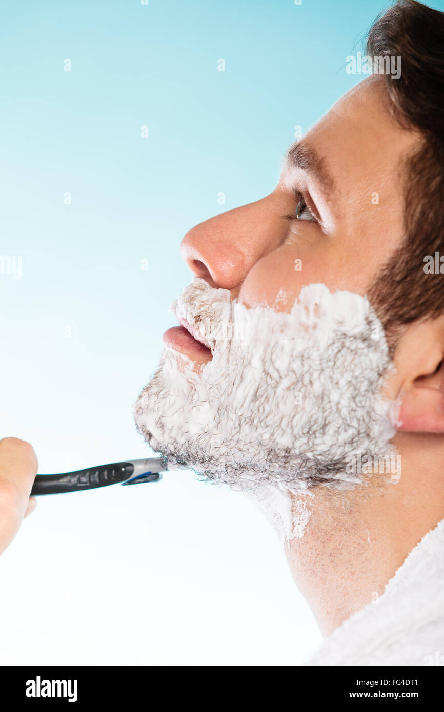 Young man shaving using razor with cream foam. Handsome guy removing face beard hair. Skin care ...