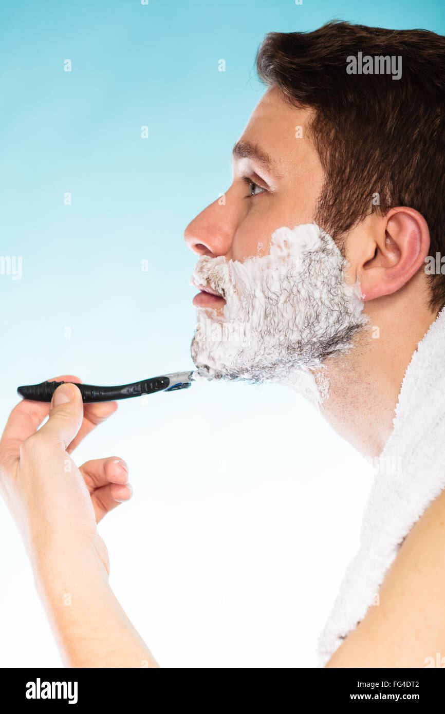 Young man shaving using razor with cream foam. Handsome guy removing face beard hair. Skin care ...