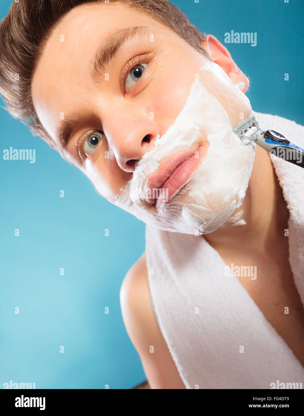 Young man shaving using razor with cream foam. Handsome guy removing face beard hair. Skin care ...