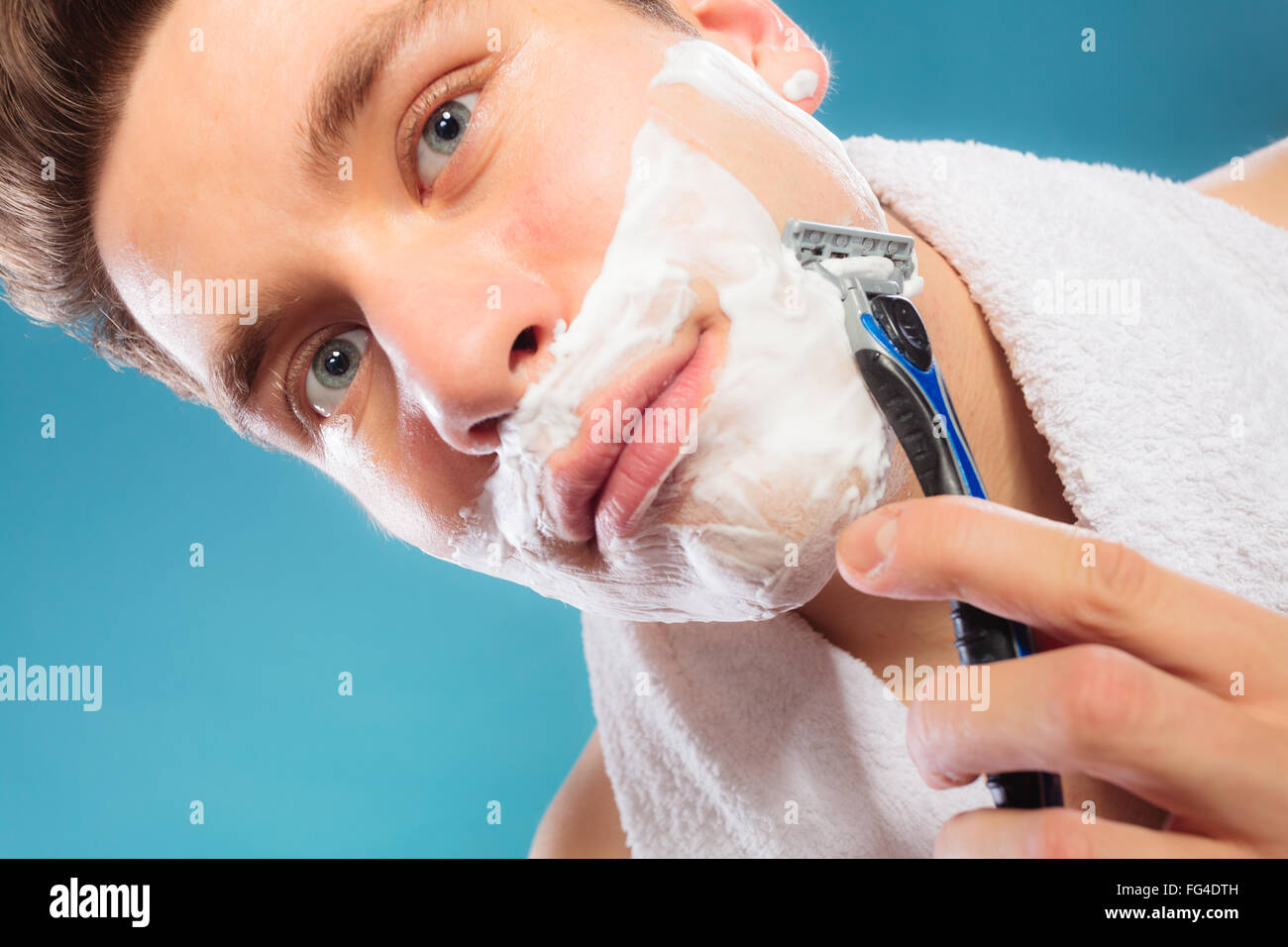 Young man shaving using razor with cream foam. Handsome guy removing face beard hair. Skin care ...