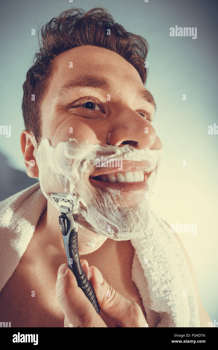 Happy smiling man shaving using razor with cream foam. Handsome guy removing beard hair. Skin ...
