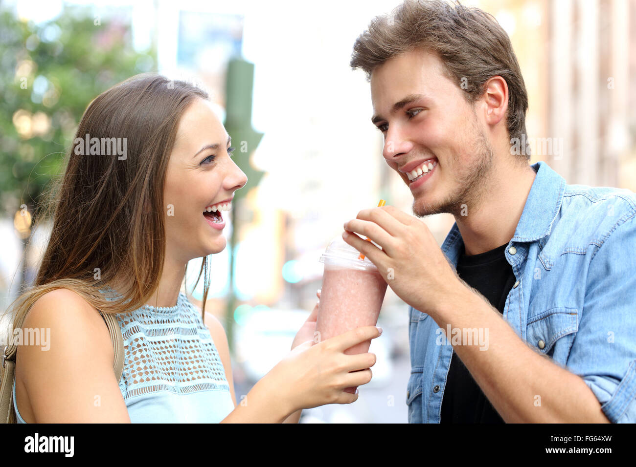 Couple or friends sharing a milkshake and laughing in the street Stock ...