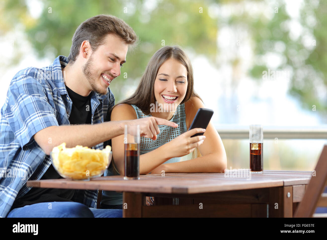 Couple sharing a smart phone sitting on a hotel or home terrace Stock ...