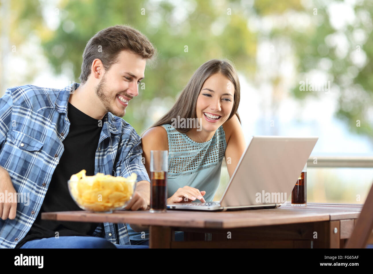 Couple watching media in a laptop sitting in an hotel or home terrace ...