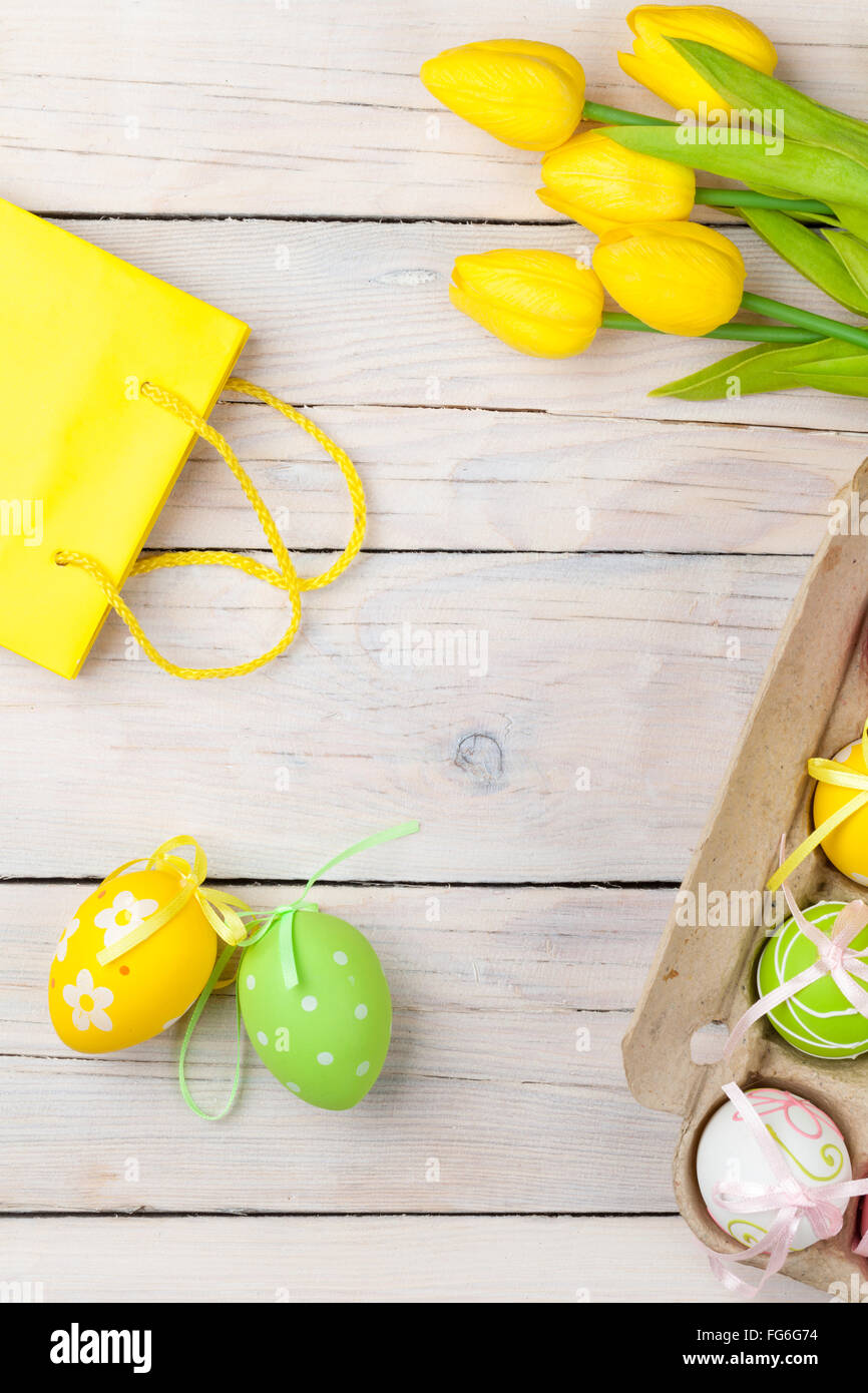 Easter background with colorful eggs and yellow tulips over white wood ...