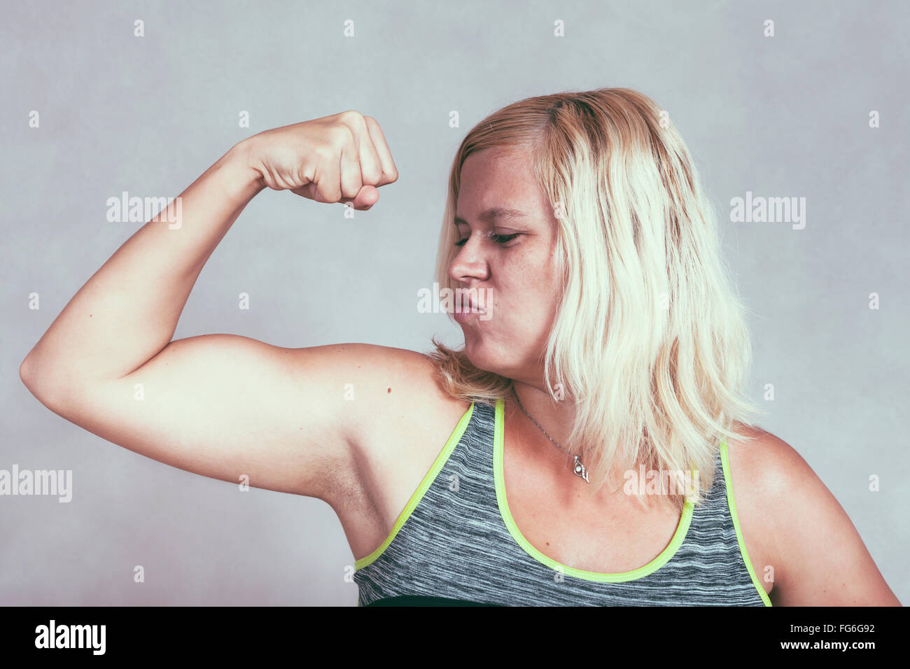 Strong confident muscular woman flexing her muscles. Young blond sporty female showing arm and ...