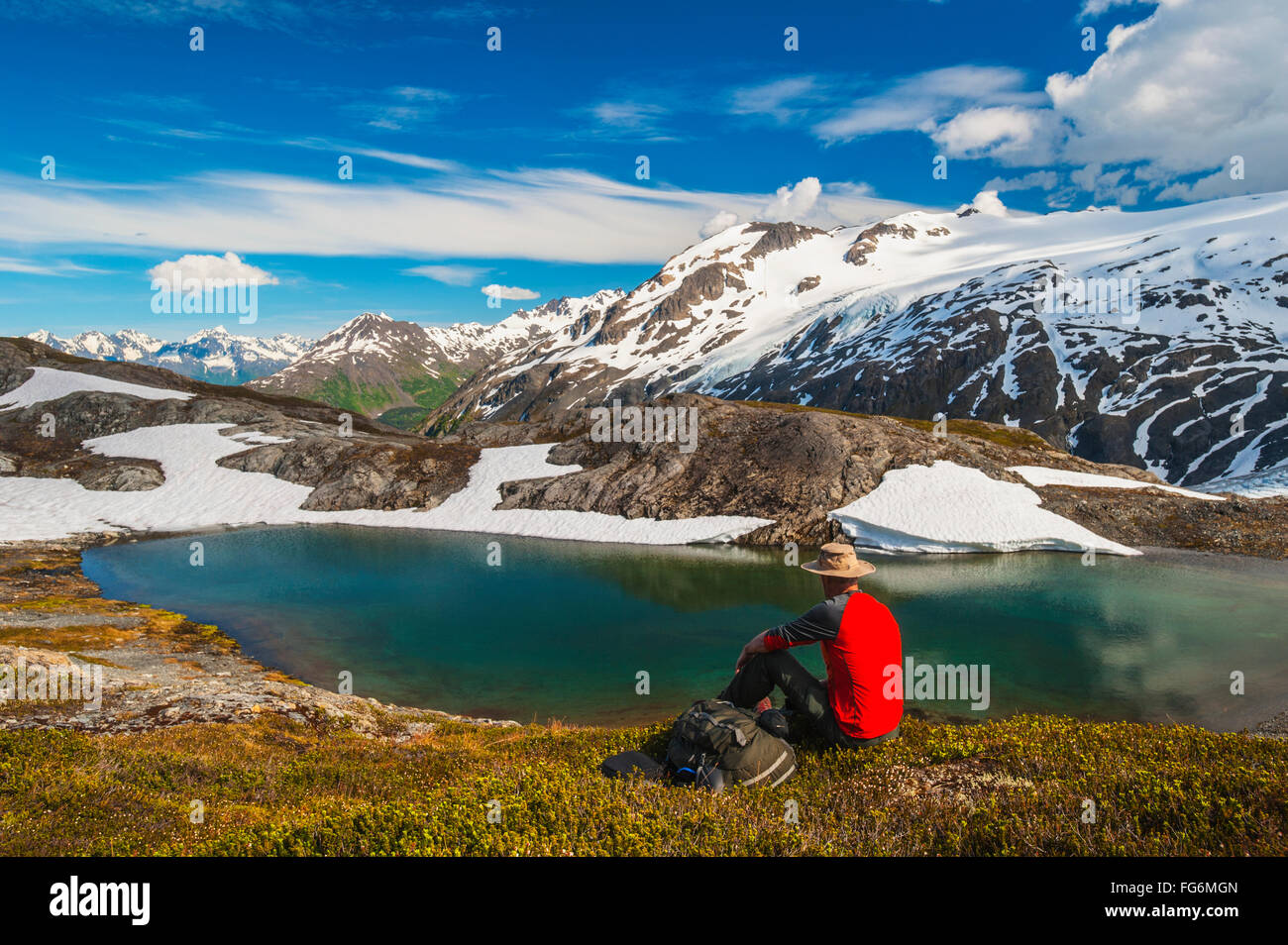 Hiker rests alongside a lake while hiking the Harding Icefield Trail ...