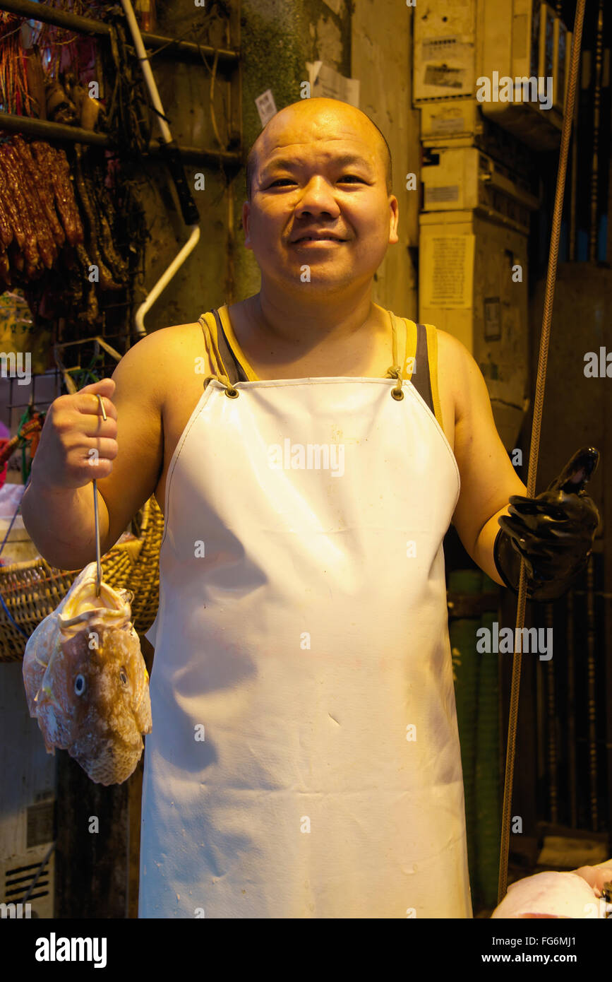 Smiling Chinese fishmonger in apron holding fish; Hong Kong, China ...