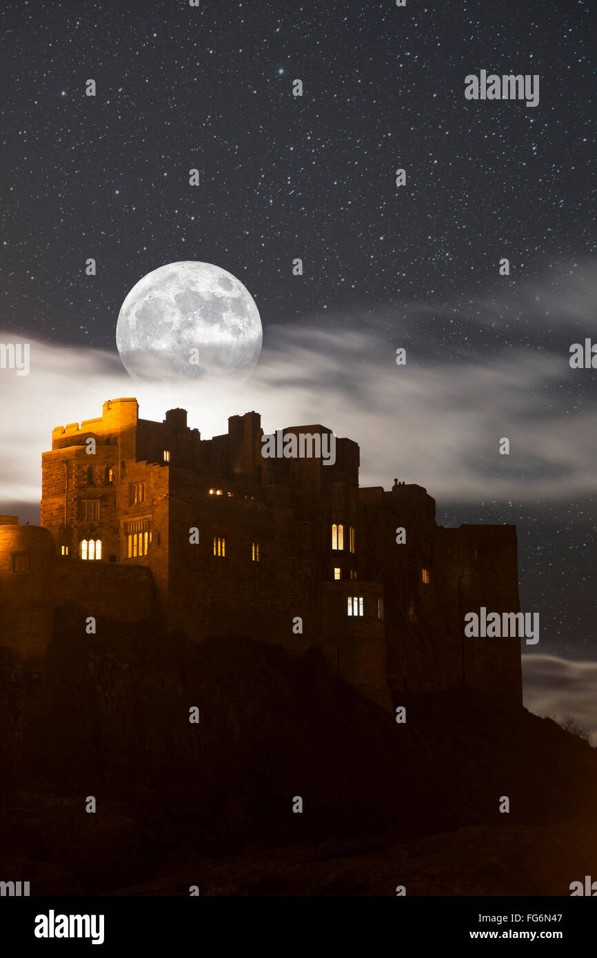 Full moon glowing in a starry sky over illuminated buildings; Bamburgh ...