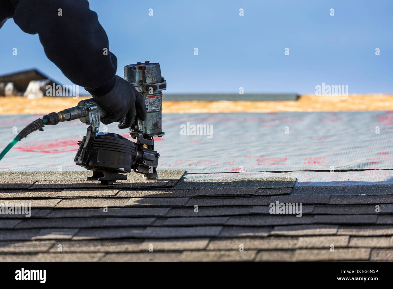 Close up of air nailer, with male roofer's hand, nailing new shingles ...