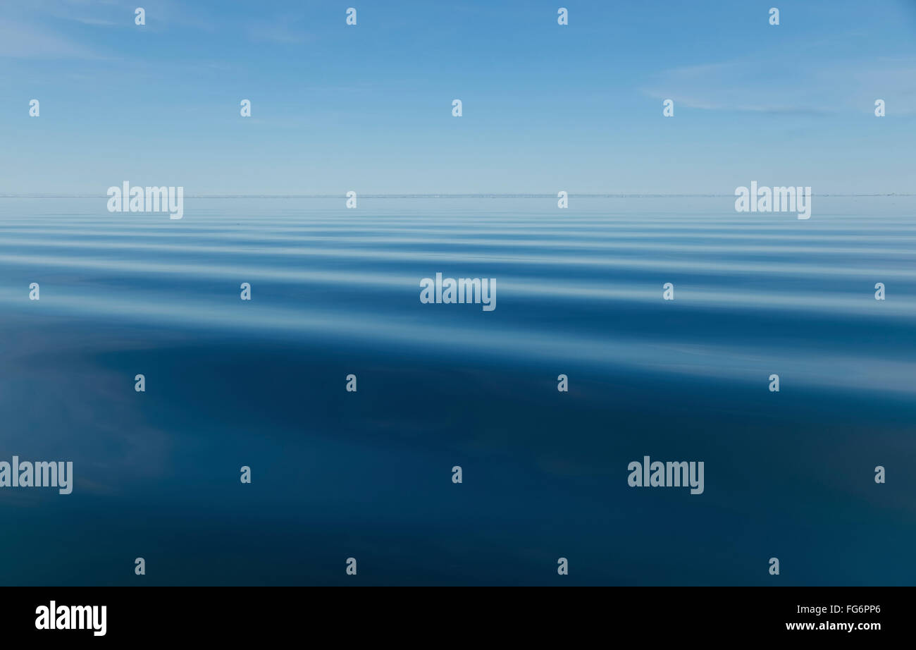 Surface of blue water with slight ripples and blue sky with horizon in ...