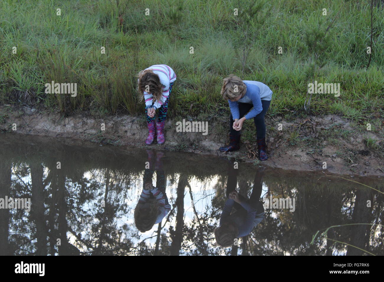 Twin children looking at reflection in water Stock Photo - Alamy