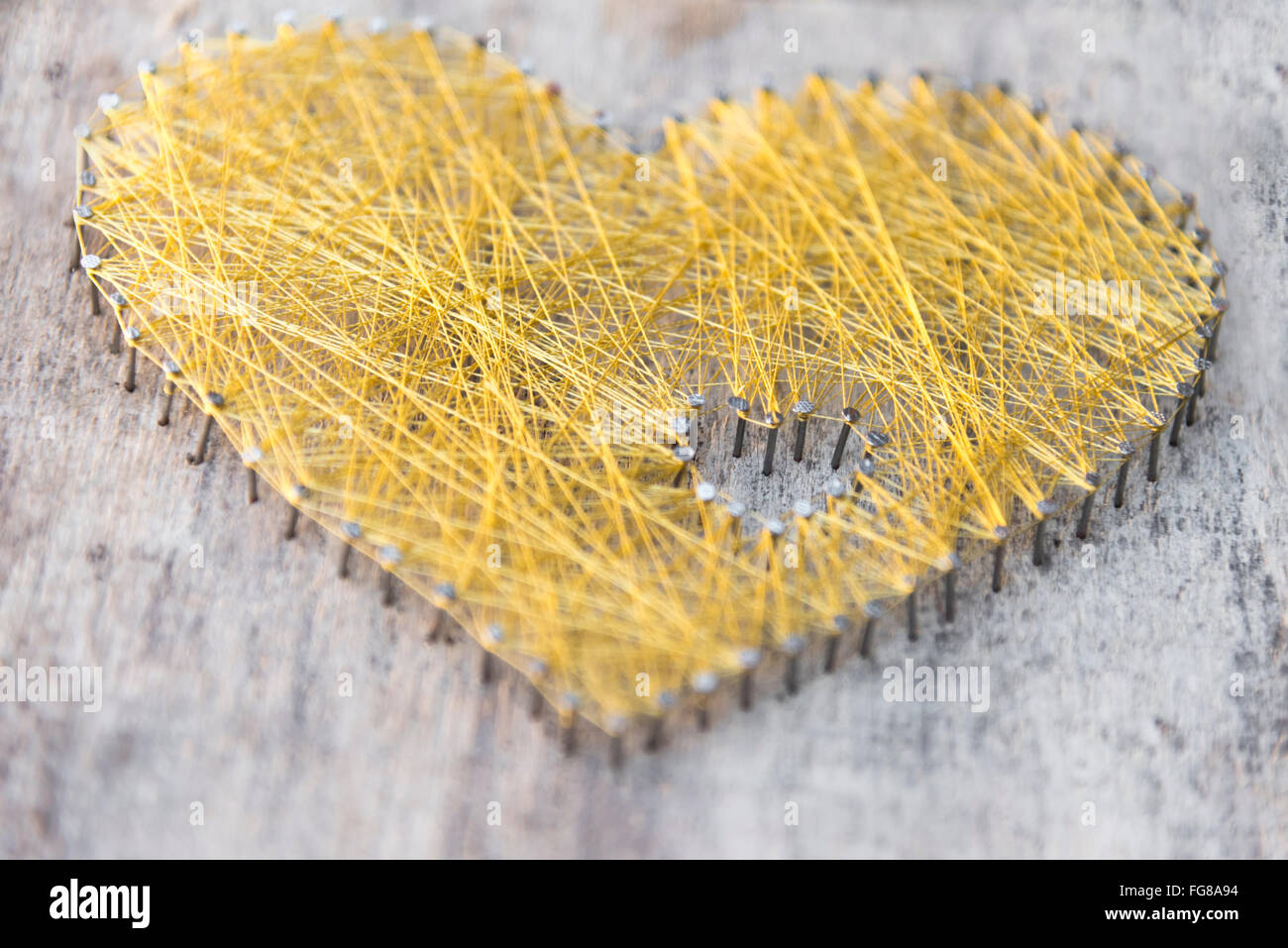 Handmade heart made of nails on wooden board with wowen gold string ...