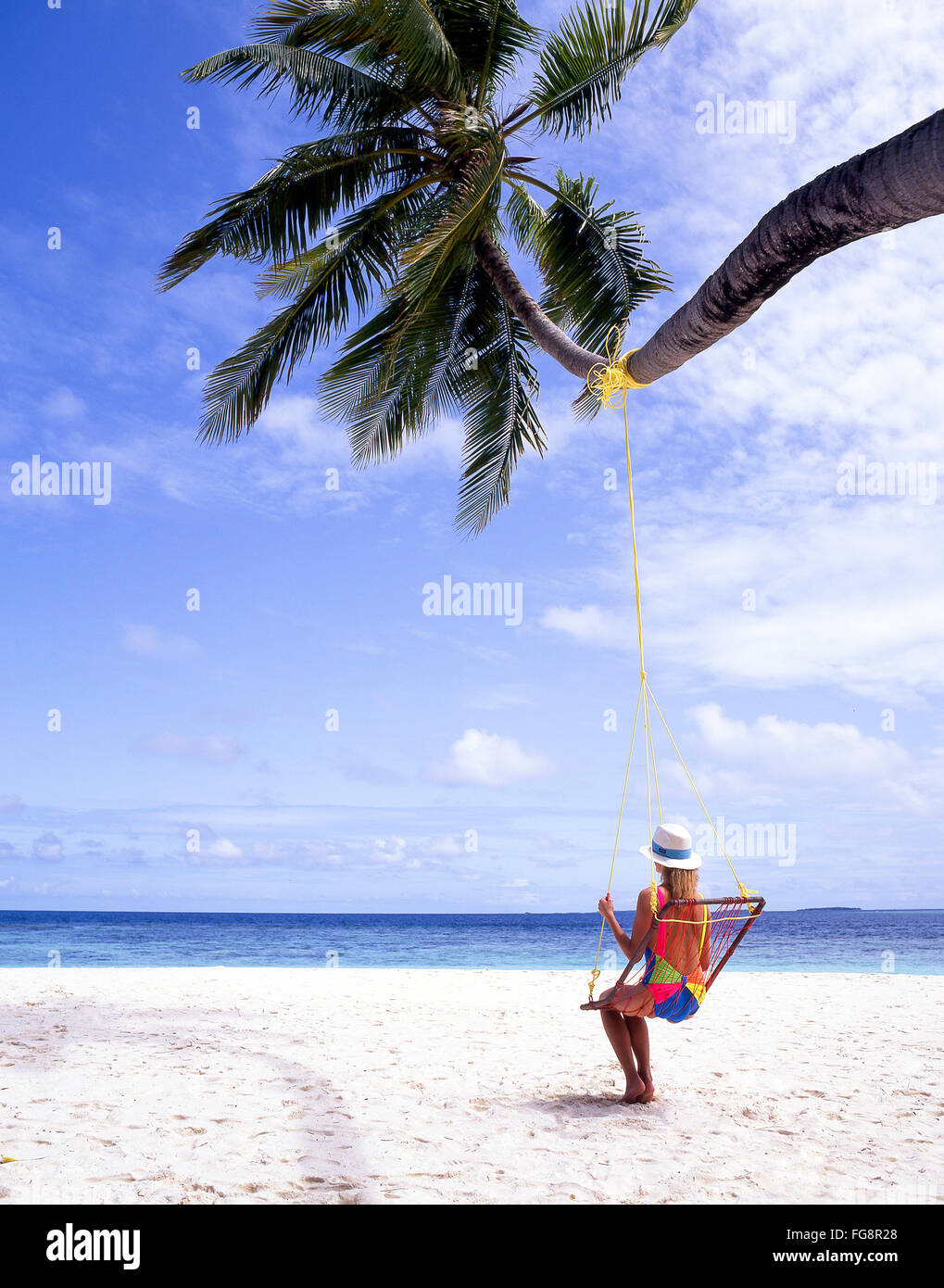 Young woman sitting beneath palm tree, Kuda Bandos, Kaafu Atoll ...