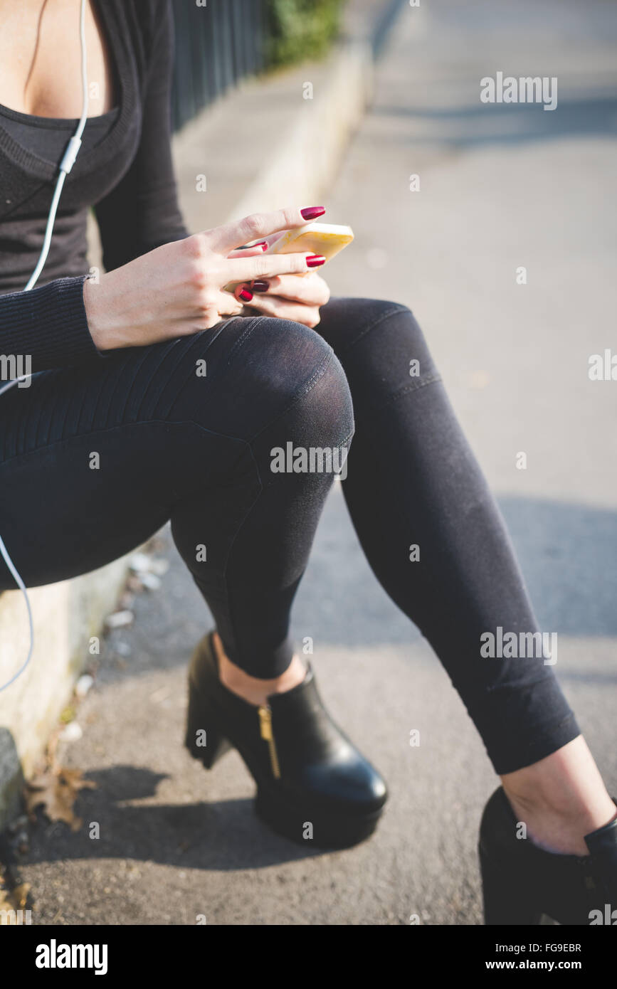From the neck down view of a woman sitting on the sidewalk holding a ...