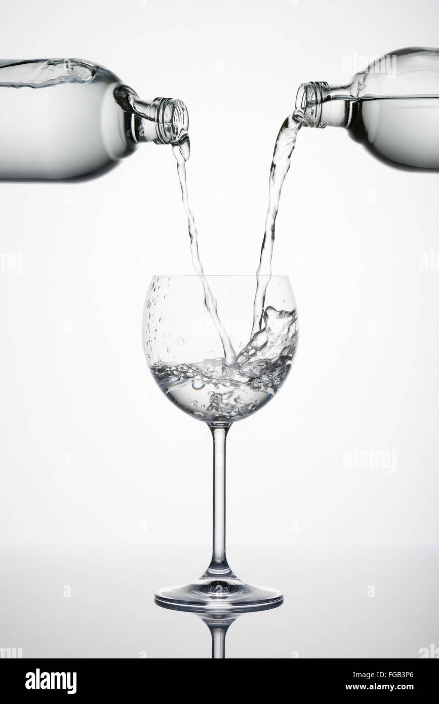 two bottles pouring water in glass with splashes on white background ...