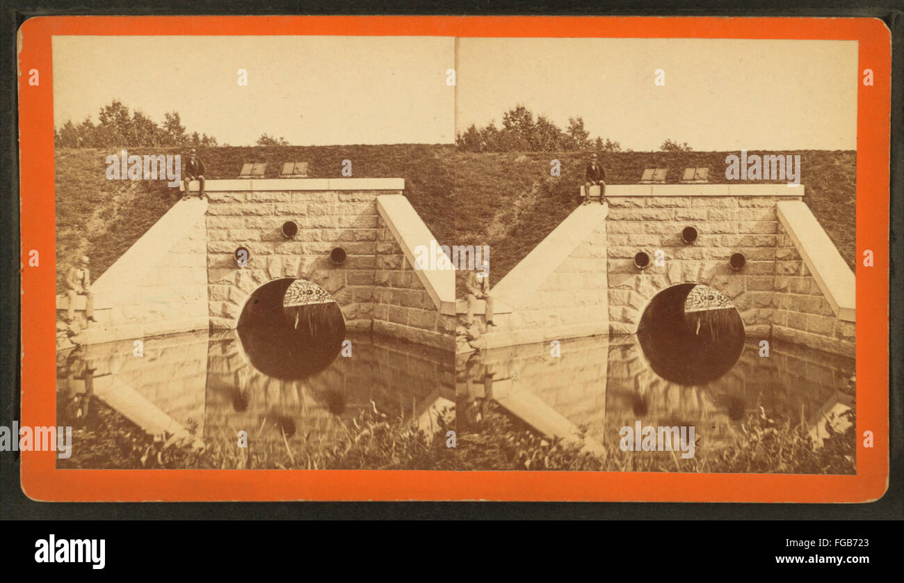 A photograph showing two people seated on a small, completed arch. The ...