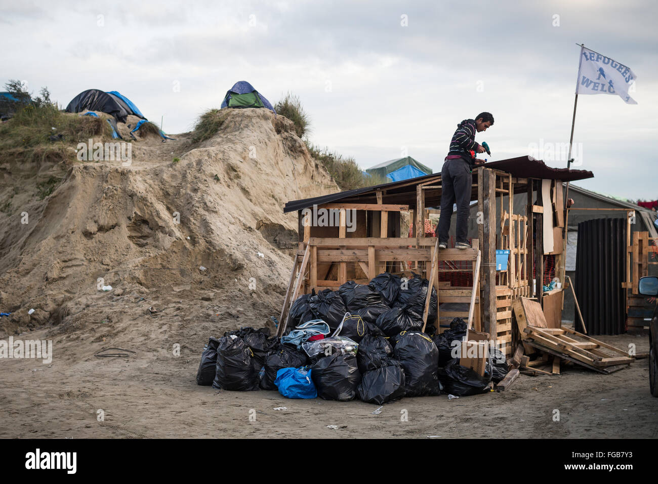 A Syrian man builds his family shelter next to a sand dune in the ...