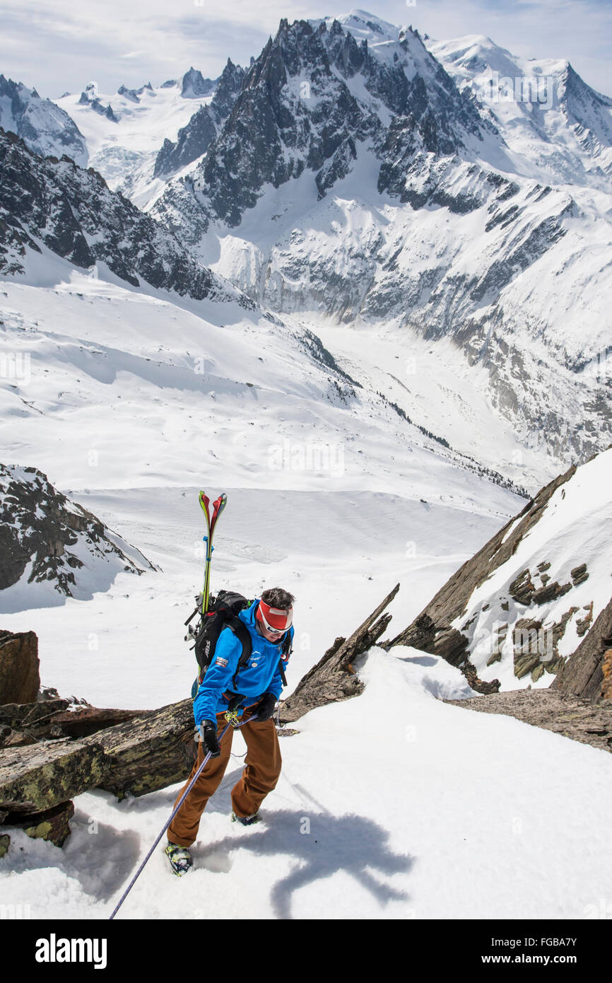 Mountain guide rappelling down with his ski on his back to reach the ...