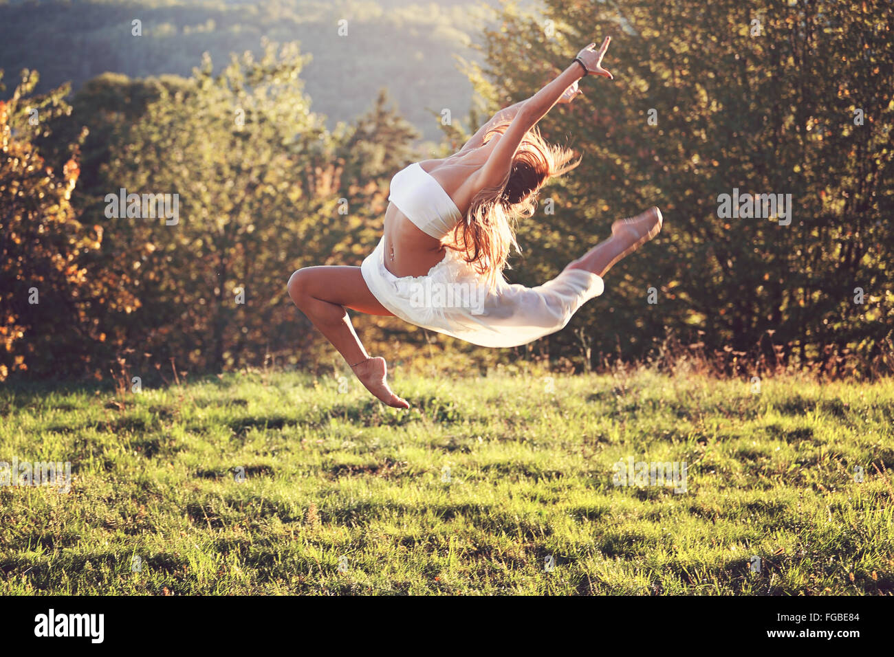 Beautiful gymnast in a difficult jump outdoor . Sunset light Stock ...