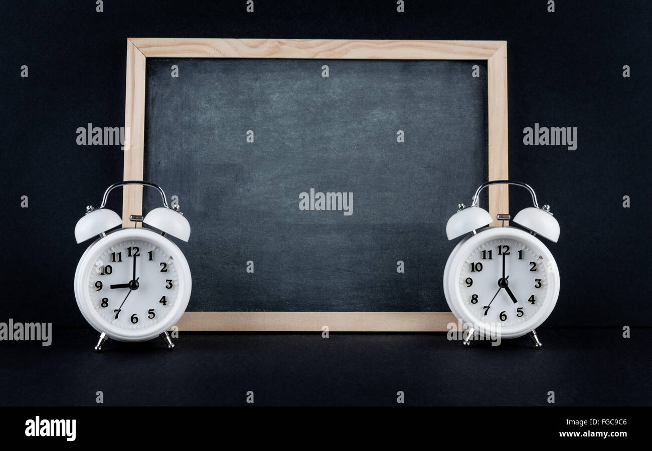 Two vintage alarm clocks showing 9 and 5 o'clock with empty chalkboard ...