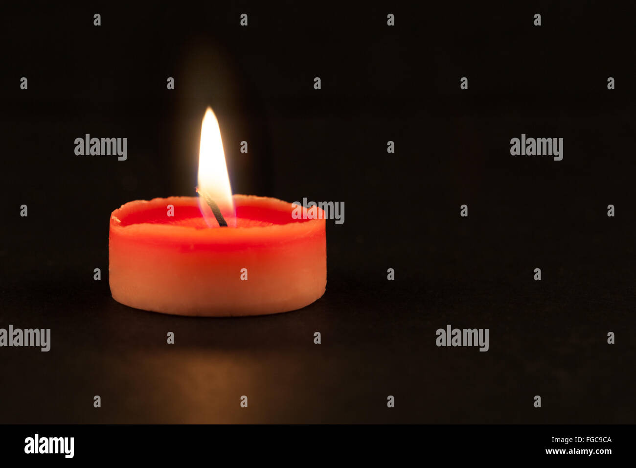 Red small candle burning on black background Stock Photo - Alamy