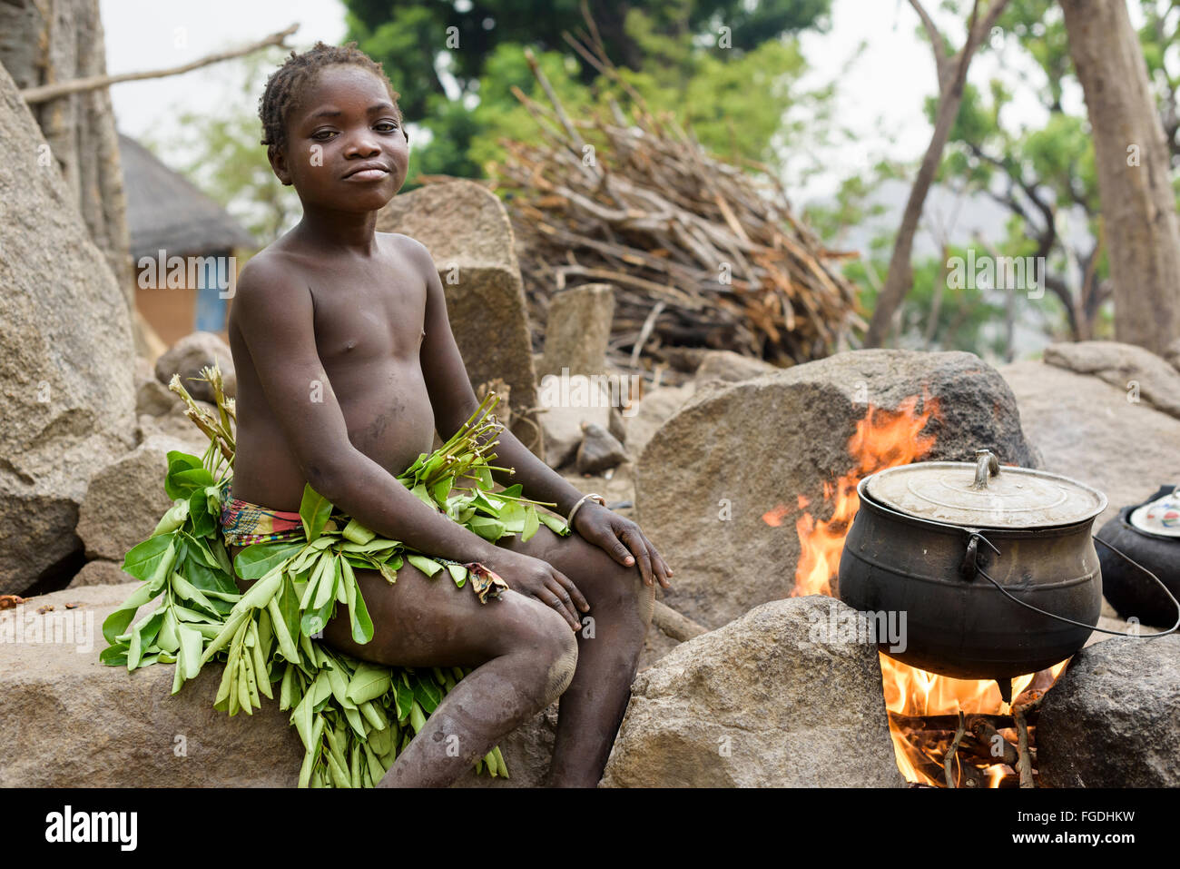 Koma girl dressed with traditional leaves dress cooking on the fire ...
