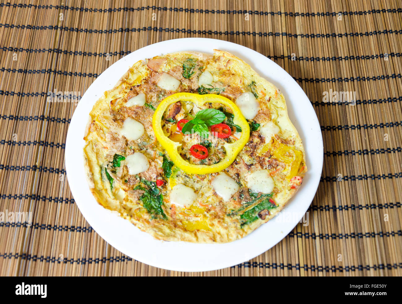 A spinach, chili, mint and pepper omelette in a dish over bamboo table ...