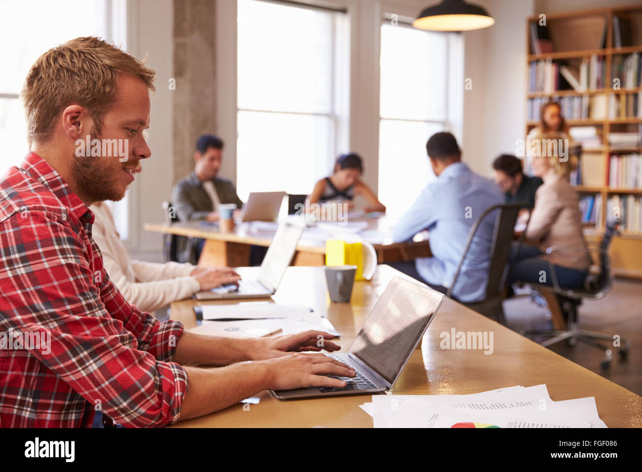 Businessman Using Laptop At Desk In Busy Office Stock Photo - Alamy