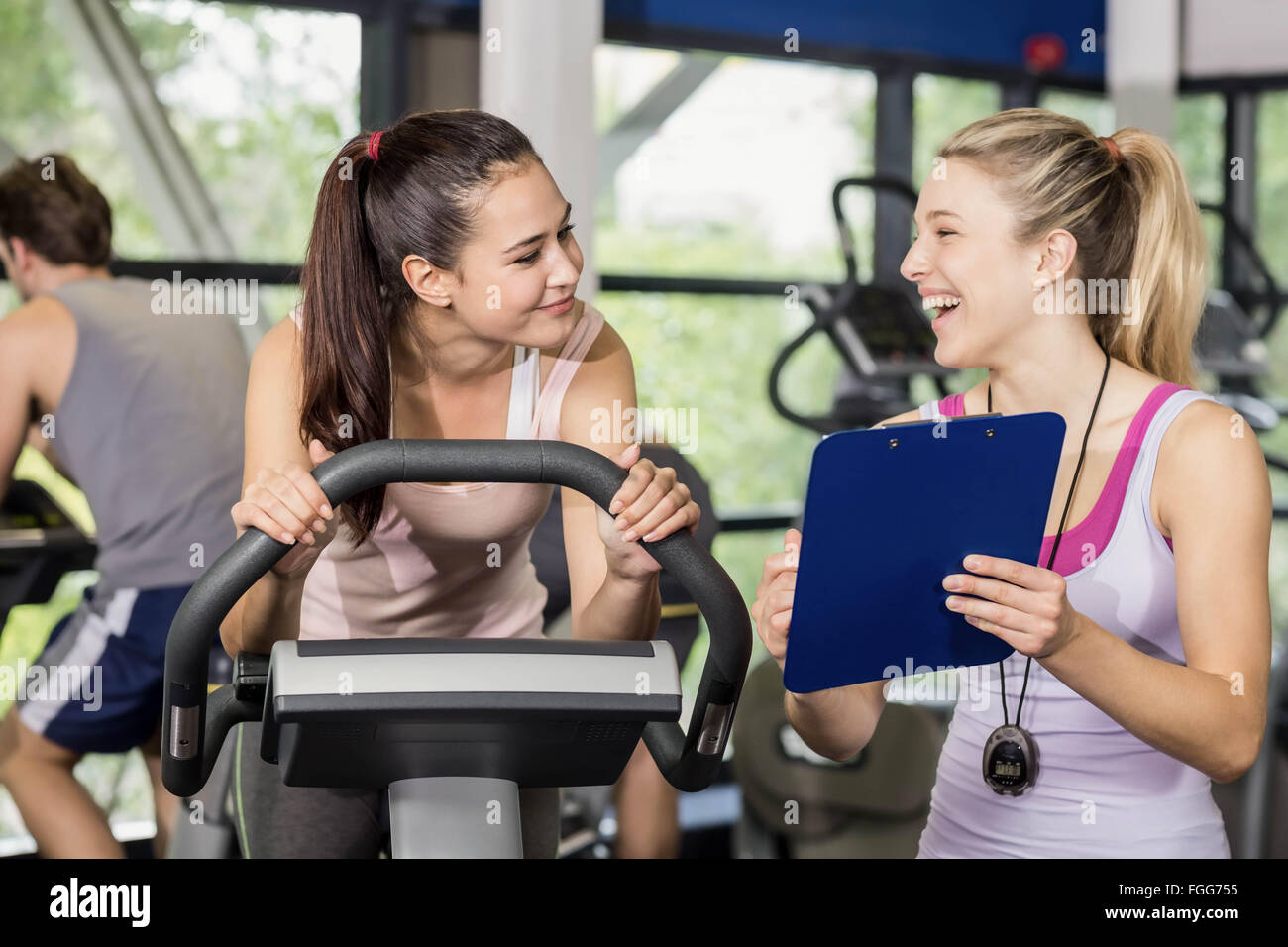 Trainer woman talking with a woman doing exercise bike Stock Photo - Alamy