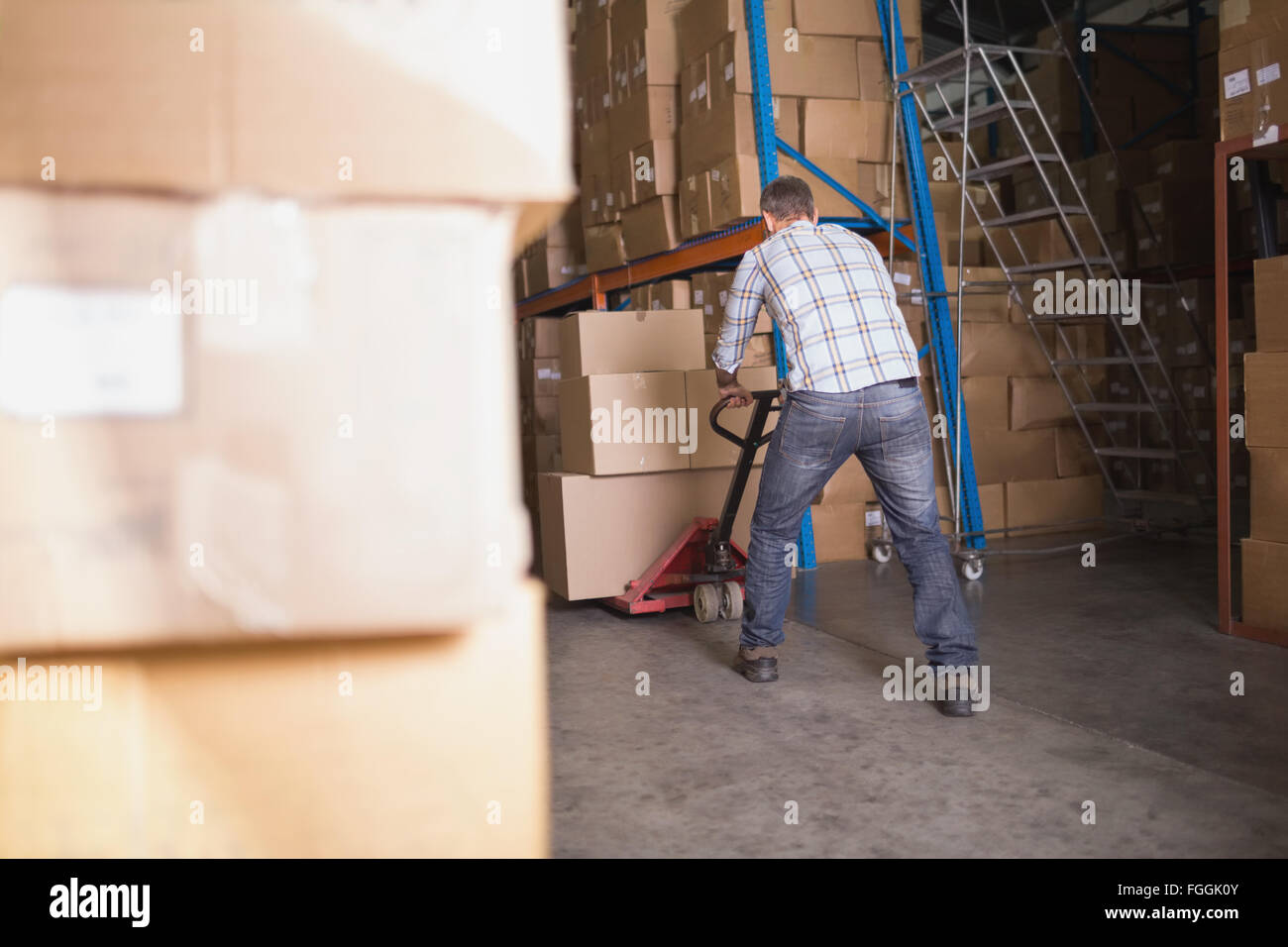 Worker pushing trolley with boxes in warehouse Stock Photo - Alamy