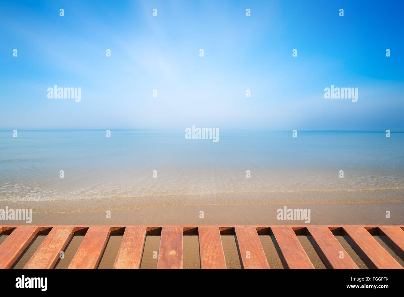 Focus on the brown wood bench with clear sand, blue beach and white ...