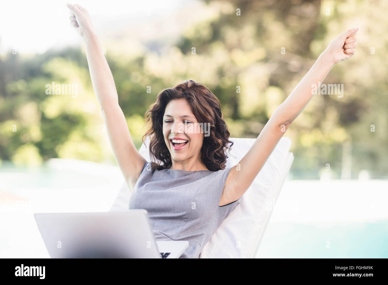 Excited young woman using laptop near poolside Stock Photo - Alamy