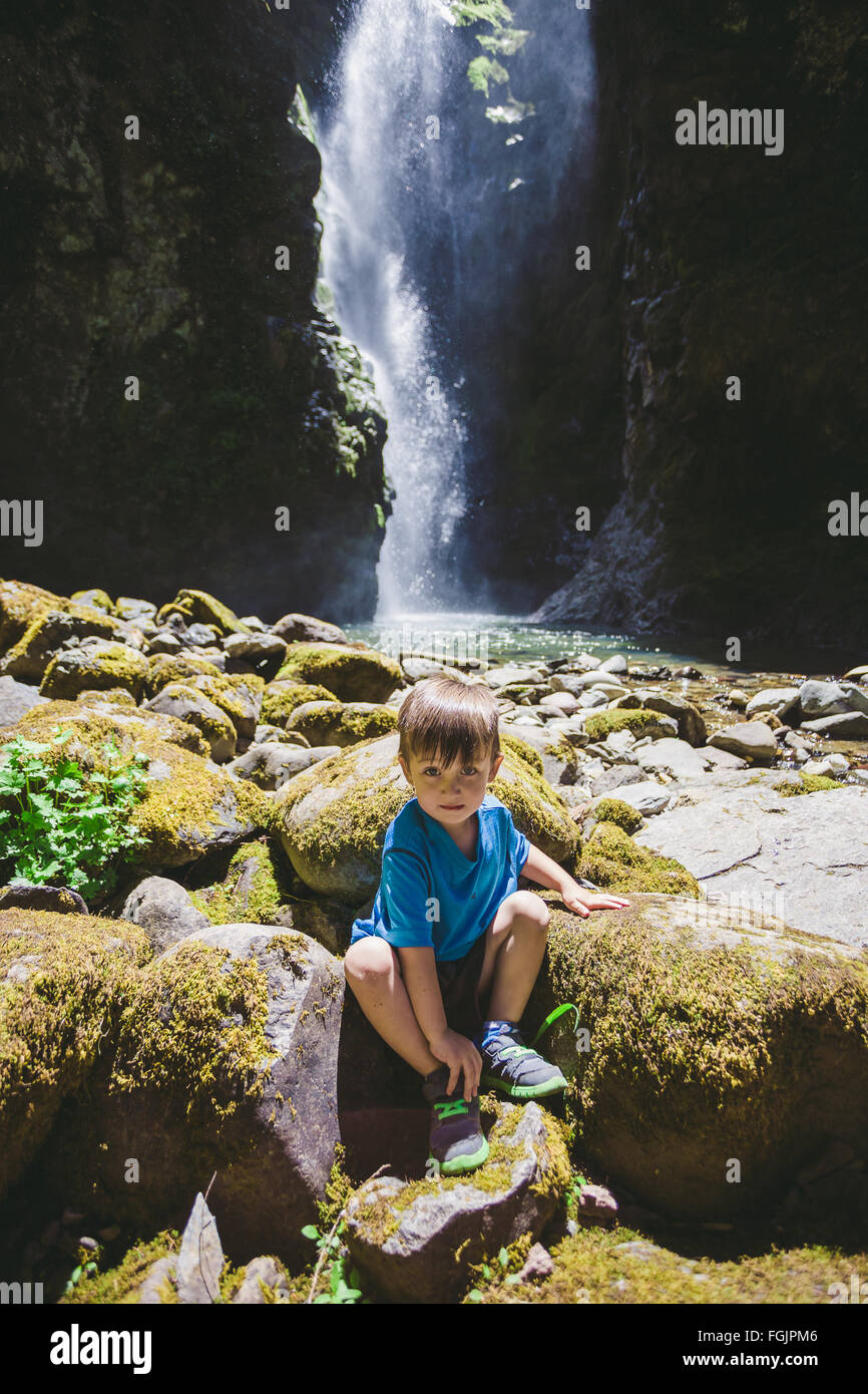 Three year old boy standing at the base of a large waterfall in the ...