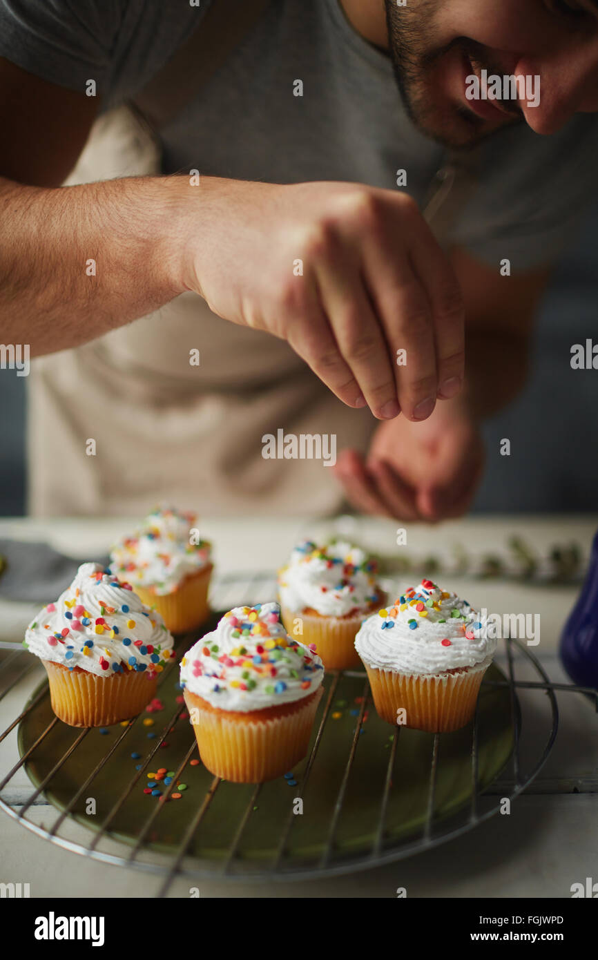 Young man decorating muffins with colorful sprinkles Stock Photo - Alamy