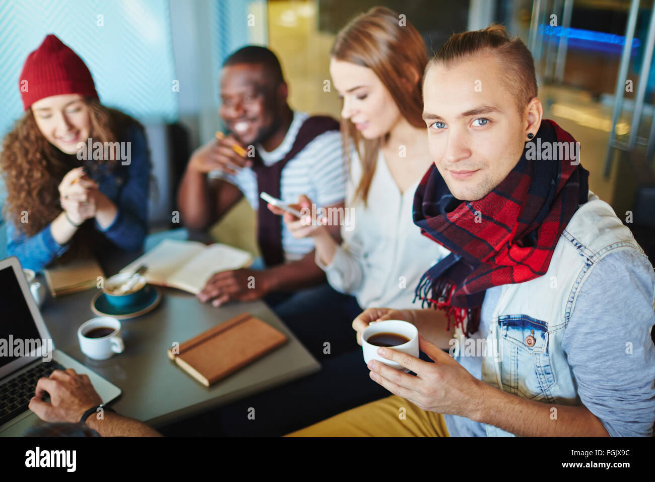 Handsome guy with cup of coffee looking at camera with his friends on ...