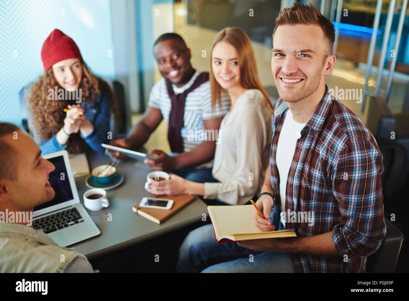 Happy guy with notepad looking at camera while his friends relaxing ...