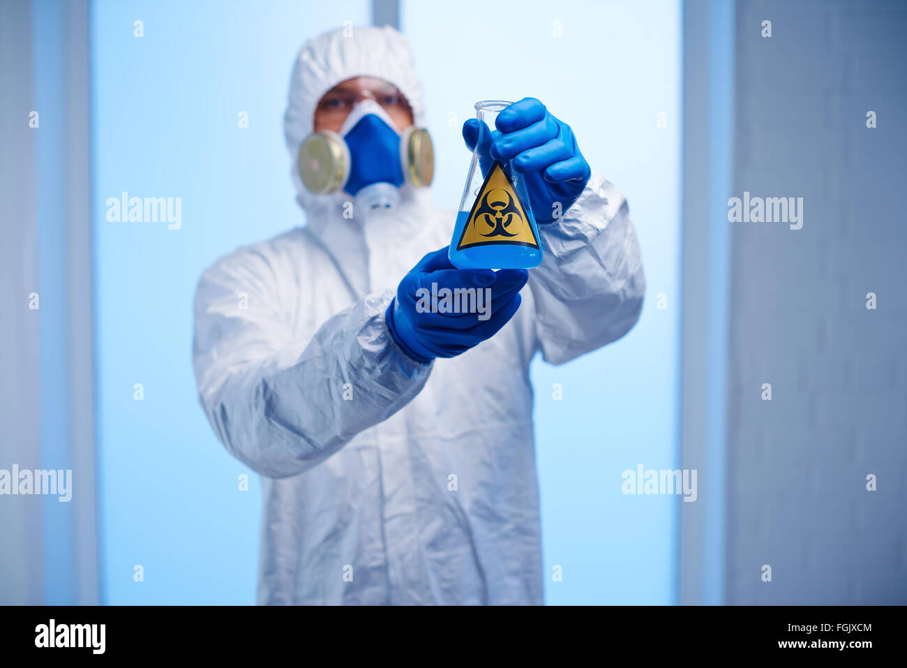 Chemist in protective overall, respirator and gloves holding flask with ...