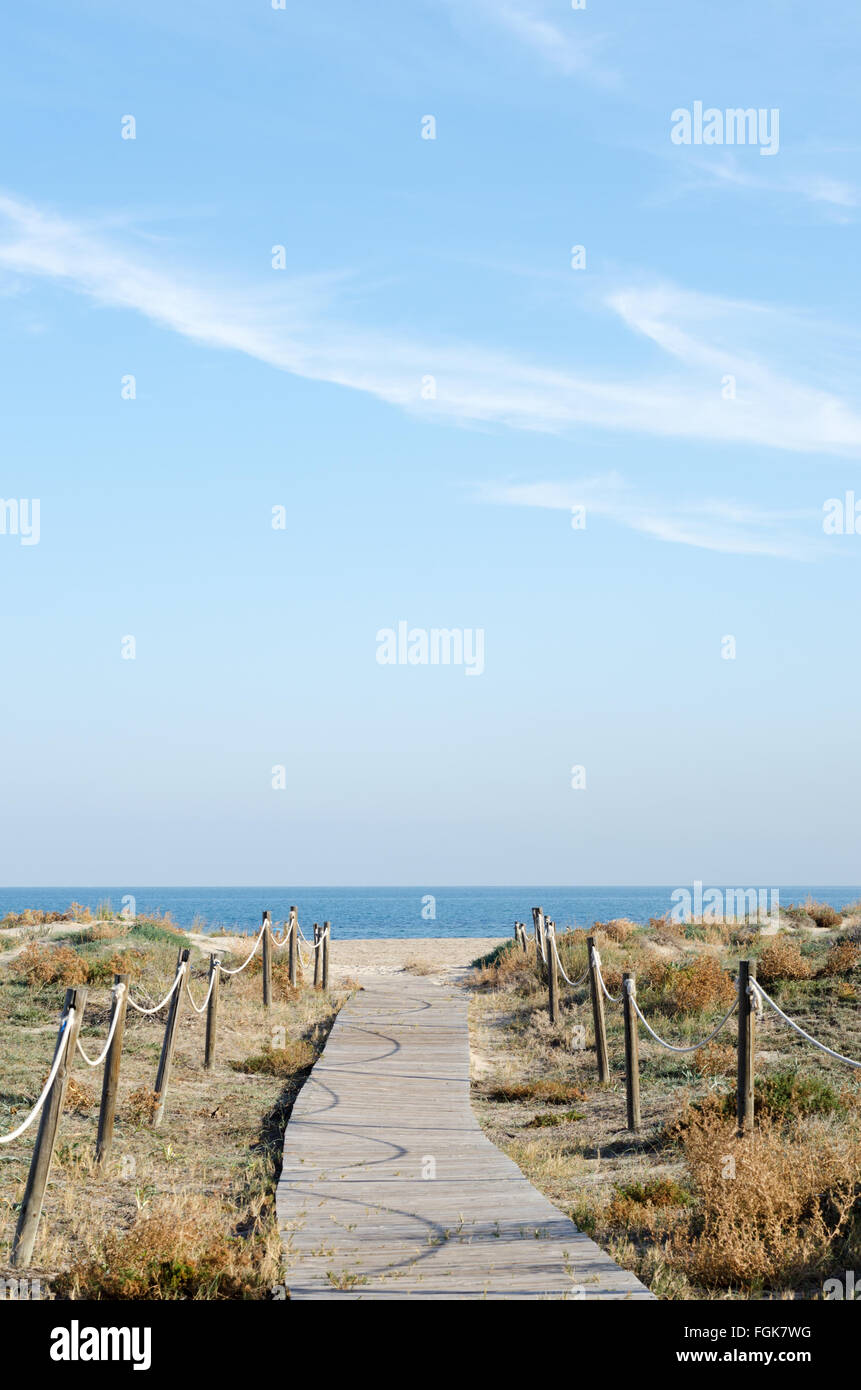 Wooden boardwalk with railing leading down to a beach and to the ocean ...