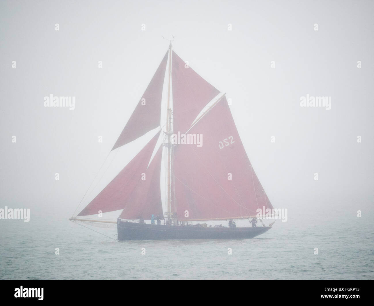 a classic yacht sails in full red sail through fog mist on a grey gray ...