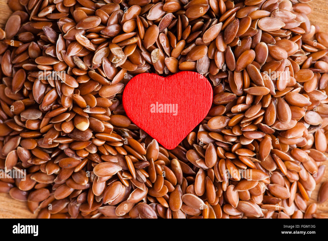 diet healthcare concept. Brown raw flax seeds linseed as natural background and red heart symbol ...
