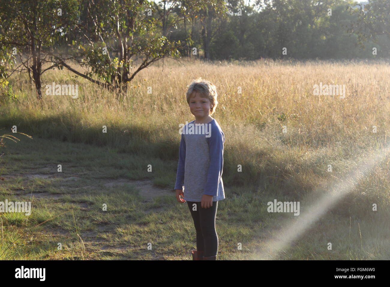 Eight year old country boy in the early morning sunshine smiling at ...