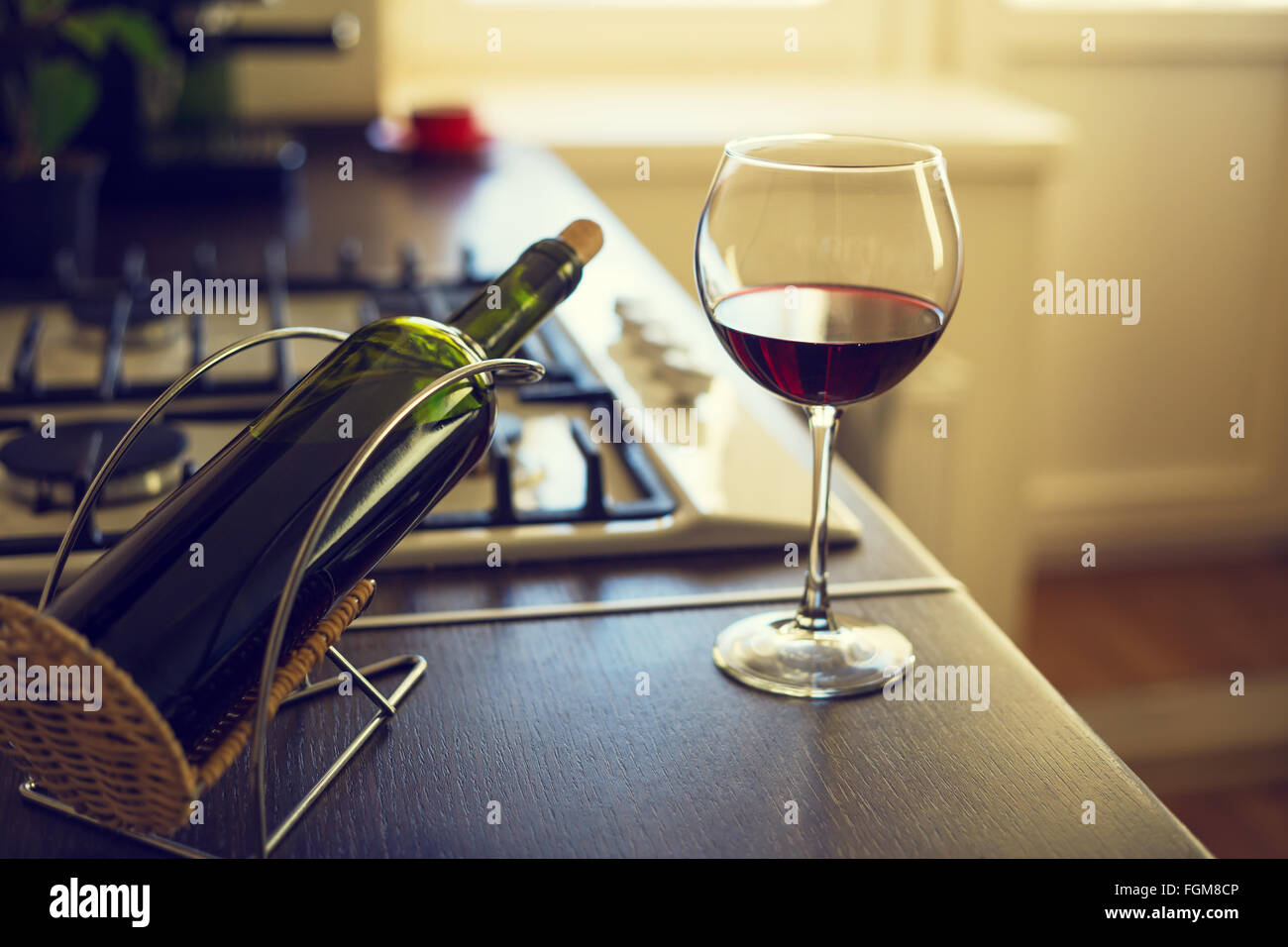 Glass of red wine with bottle near a cooker on the kitchen worktop ...