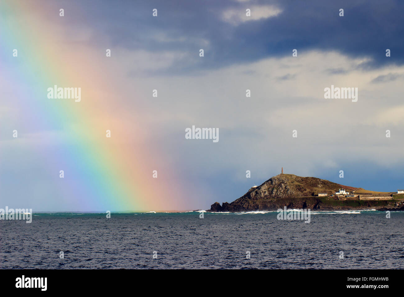 Mid February rain shower produces a rainbow over the rocky shoreline of ...
